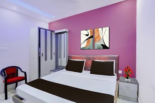 Quarto moderno com cama, poltrona, mesa de cabeceira e arte abstrata na parede.