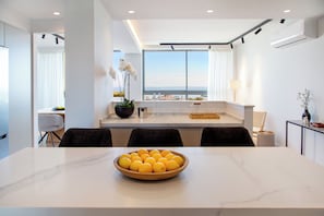 Cozinha moderna com uma janela grande, uma mesa de jantar com uma tigela de frutas e vista para o mar.