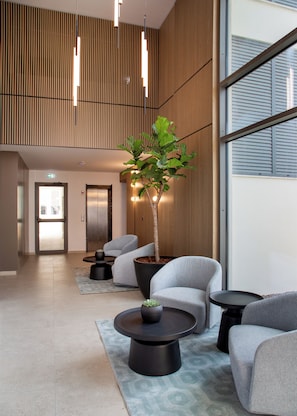 Um lobby moderno com uma grande planta em vaso, assentos confortáveis e entrada por porta de vidro.