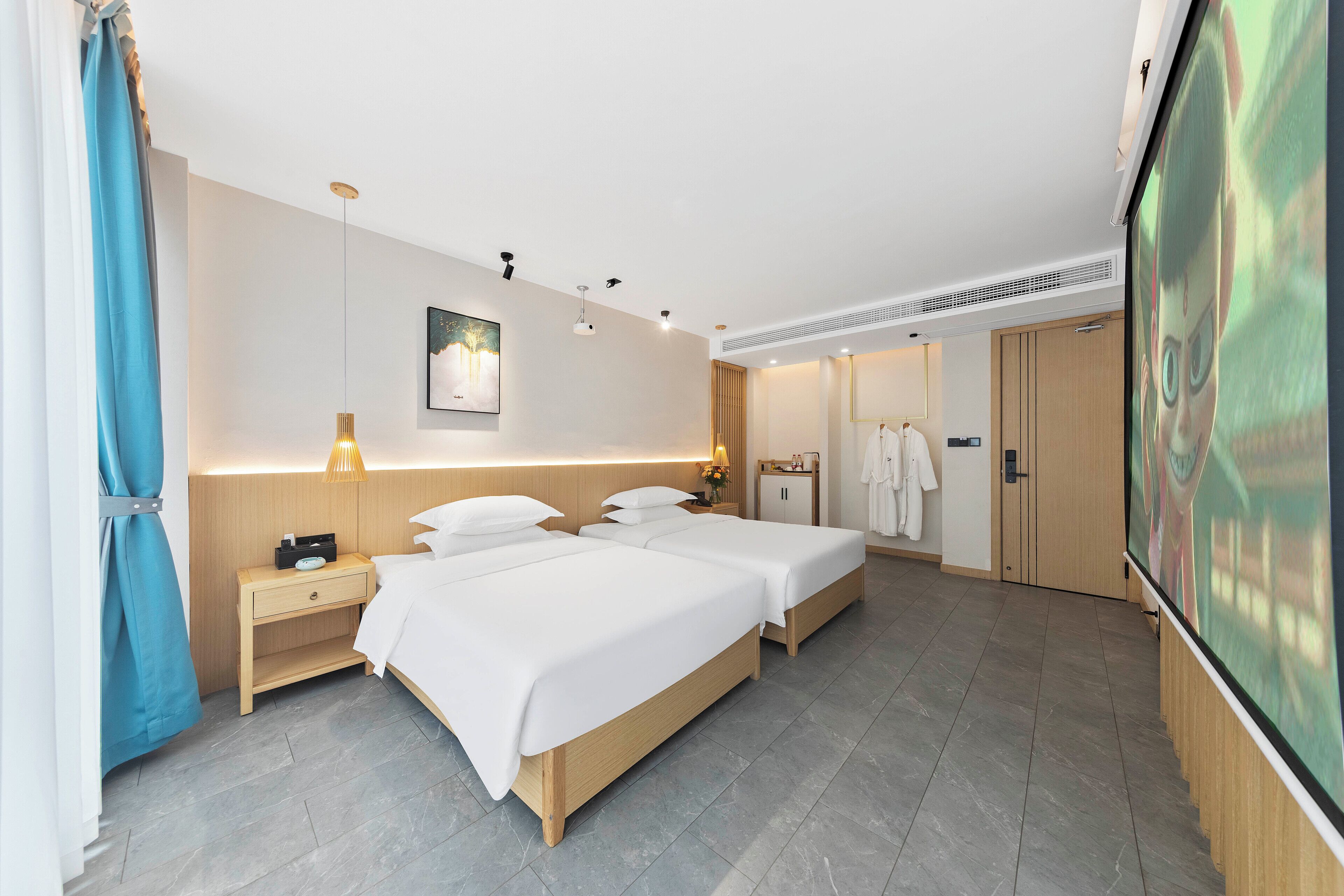 Quarto de hotel com duas camas, mesa de cabeceira, escrivaninha, guarda-roupa e uma grande televisão.