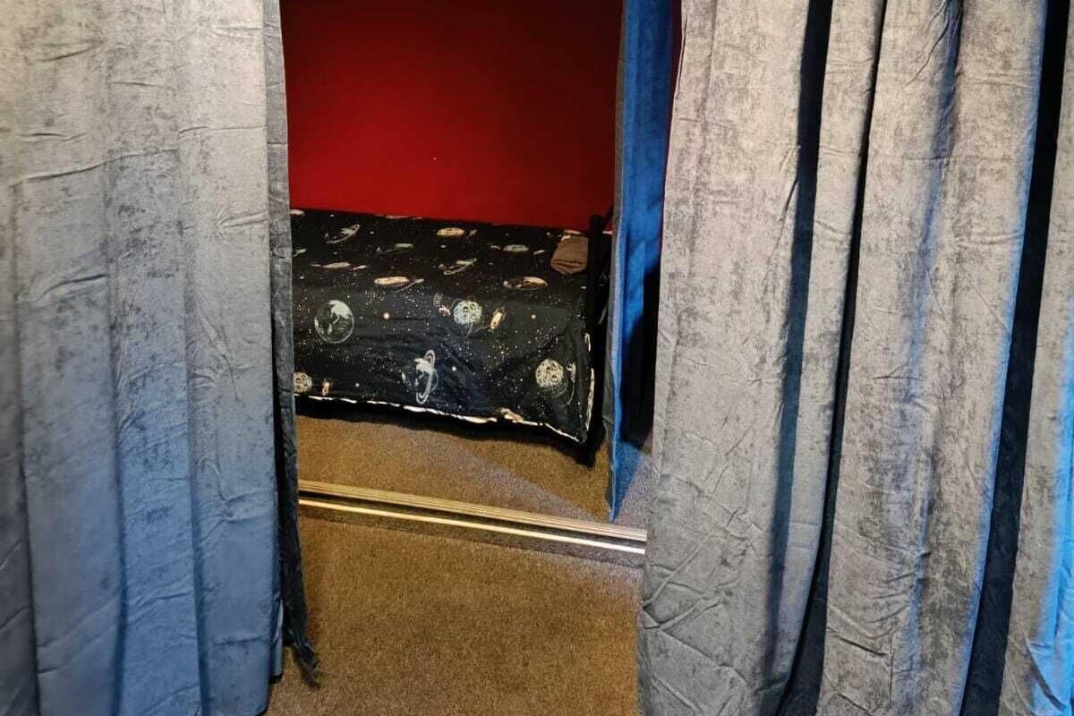 Quarto com parede vermelha, cama com colcha estampada em preto e branco e cortinas cinzas.
