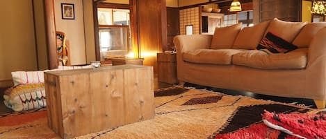 Uma sala de estar em estilo japonês tradicional, com tatames, uma mesa de centro de madeira baixa e um sofá bege com almofadas.