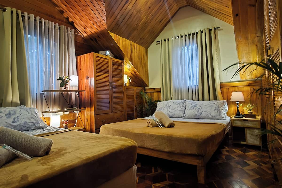 Quarto aconchegante com duas camas, teto de madeira e uma pequena mesa com abajur.