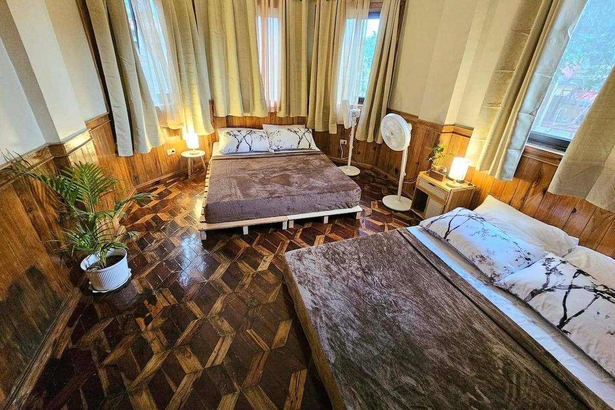 Quarto com uma cama, um banco, um ventilador e um vaso com planta.