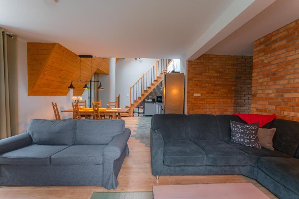 Uma sala de estar moderna com dois sofás, uma mesa de jantar e uma escada que leva a um andar superior.