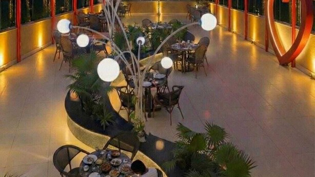 Área de refeições no terraço, com mesas, cadeiras e uma estrutura luminosa decorativa.