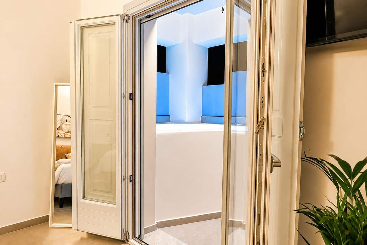 Quarto de hotel com porta deslizante para um banheiro, uma cama, um espelho e um vaso de planta.