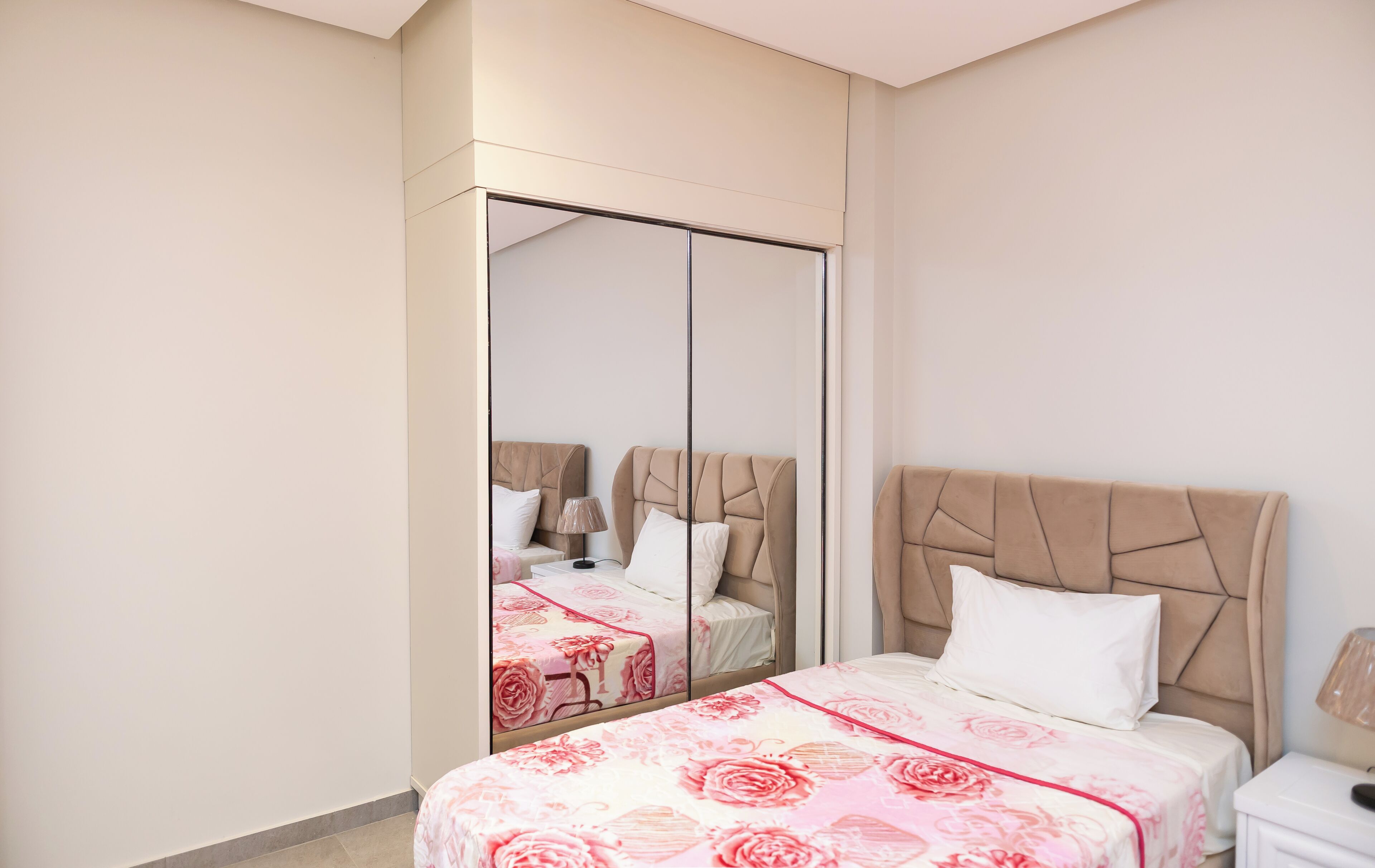 Quarto com cama, mesa de cabeceira, espelho e guarda-roupa.