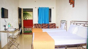 Quarto de hotel com uma cama, uma secretária com cadeira, televisão e janela com cortinas.