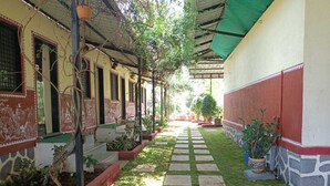Uma área externa coberta com um caminho, plantas em vasos e um edifício com entrada em azulejo.