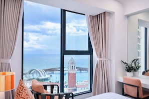 Quarto de hotel com uma janela grande, uma cama, uma cadeira, um abajur e um vaso de plantas.
