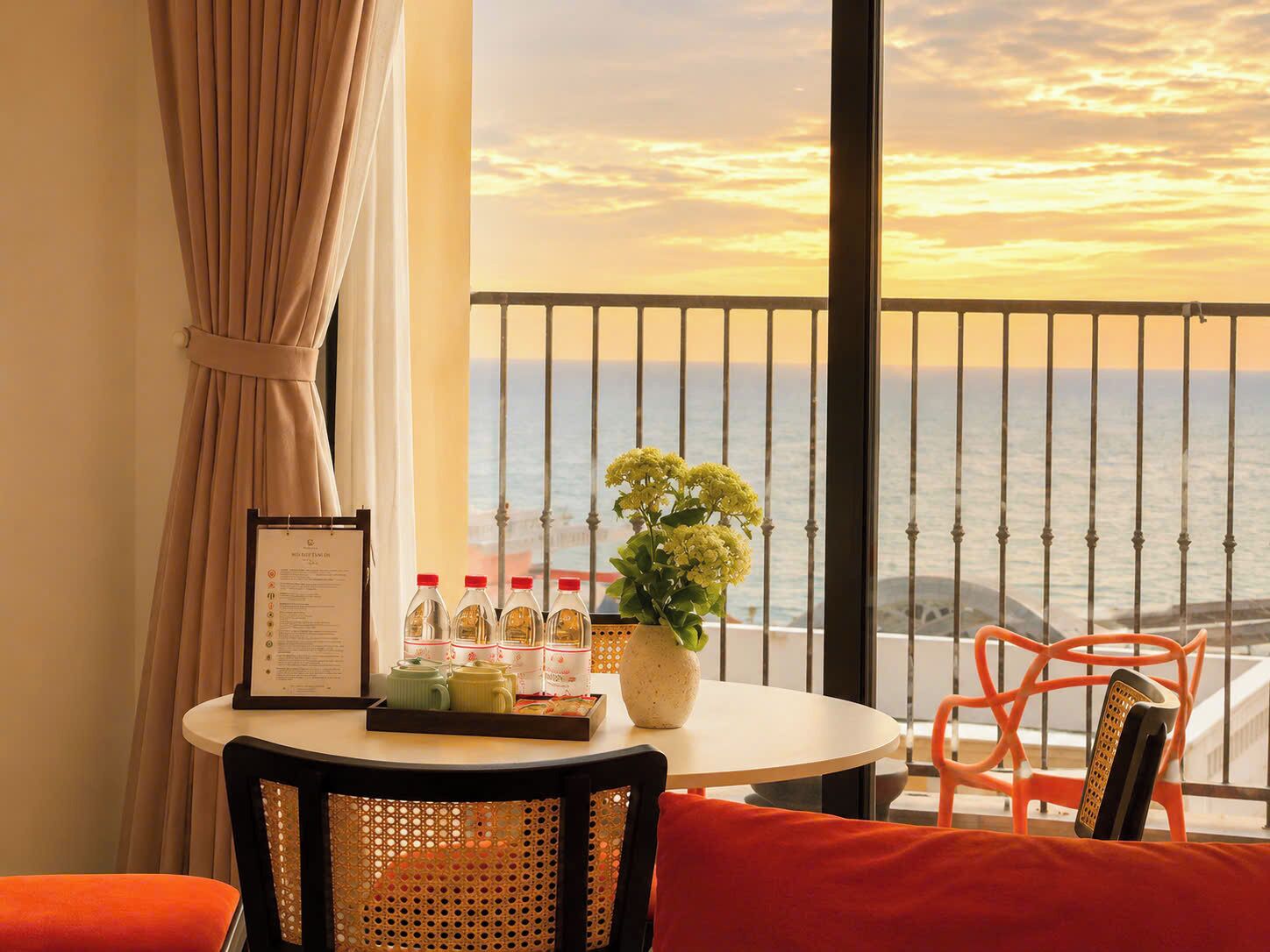 Quarto de hotel com varanda, uma mesa com cardápio e vista para o mar.