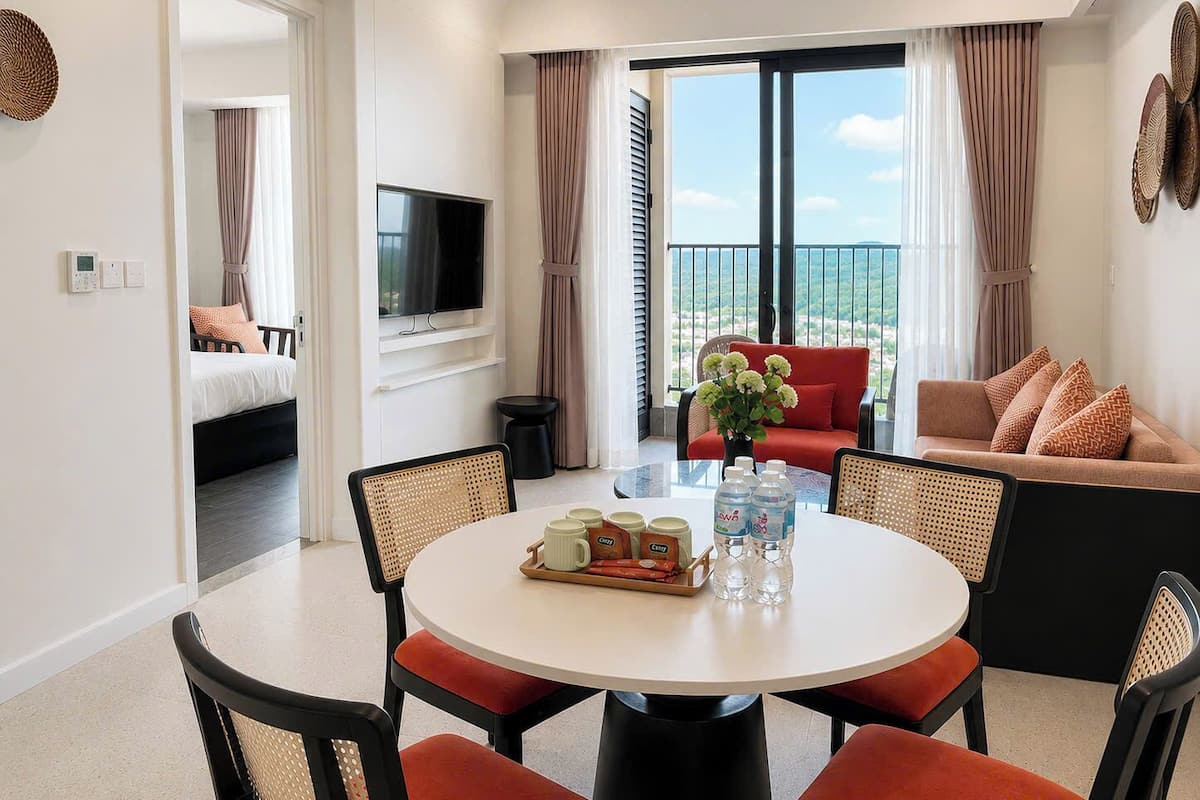 Quarto de hotel moderno com varanda, área de jantar com mesa redonda e um sofá.