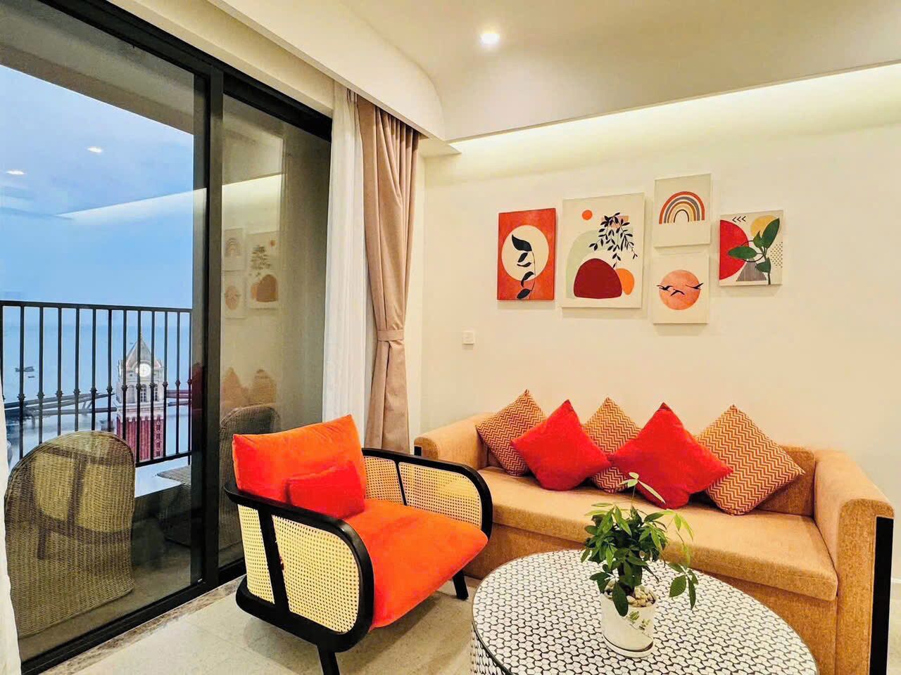 Uma sala de estar moderna com sofá, poltrona e mesa de centro redonda, varanda com vista e arte abstrata na parede.