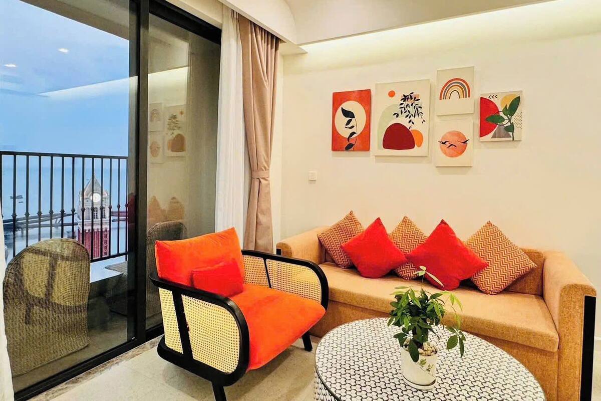 Uma sala de estar moderna com sofá, poltrona e mesa de centro redonda, varanda com vista e arte abstrata na parede.