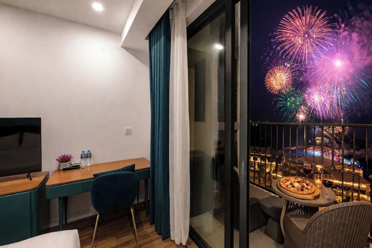 Quarto de hotel com varanda, escrivaninha, cadeira, cama e televisão.