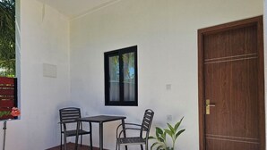 Um pátio externo com uma mesa, duas cadeiras, um vaso de planta e uma porta de madeira.