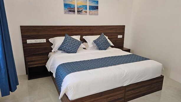 Cama bem arrumada com cabeceira de madeira, edredom azul e branco e dois travesseiros iguais.