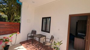 Um pátio com uma mesa, duas cadeiras, uma janela e uma porta que dá para o interior.