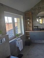Casa de banho com janela, porta-toalhas, pia, espelho e prateleiras com artigos de higiene pessoal.