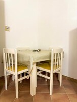 Mesa de jantar com toalha, duas cadeiras com almofadas amarelas e um interruptor de luz fixado na parede.