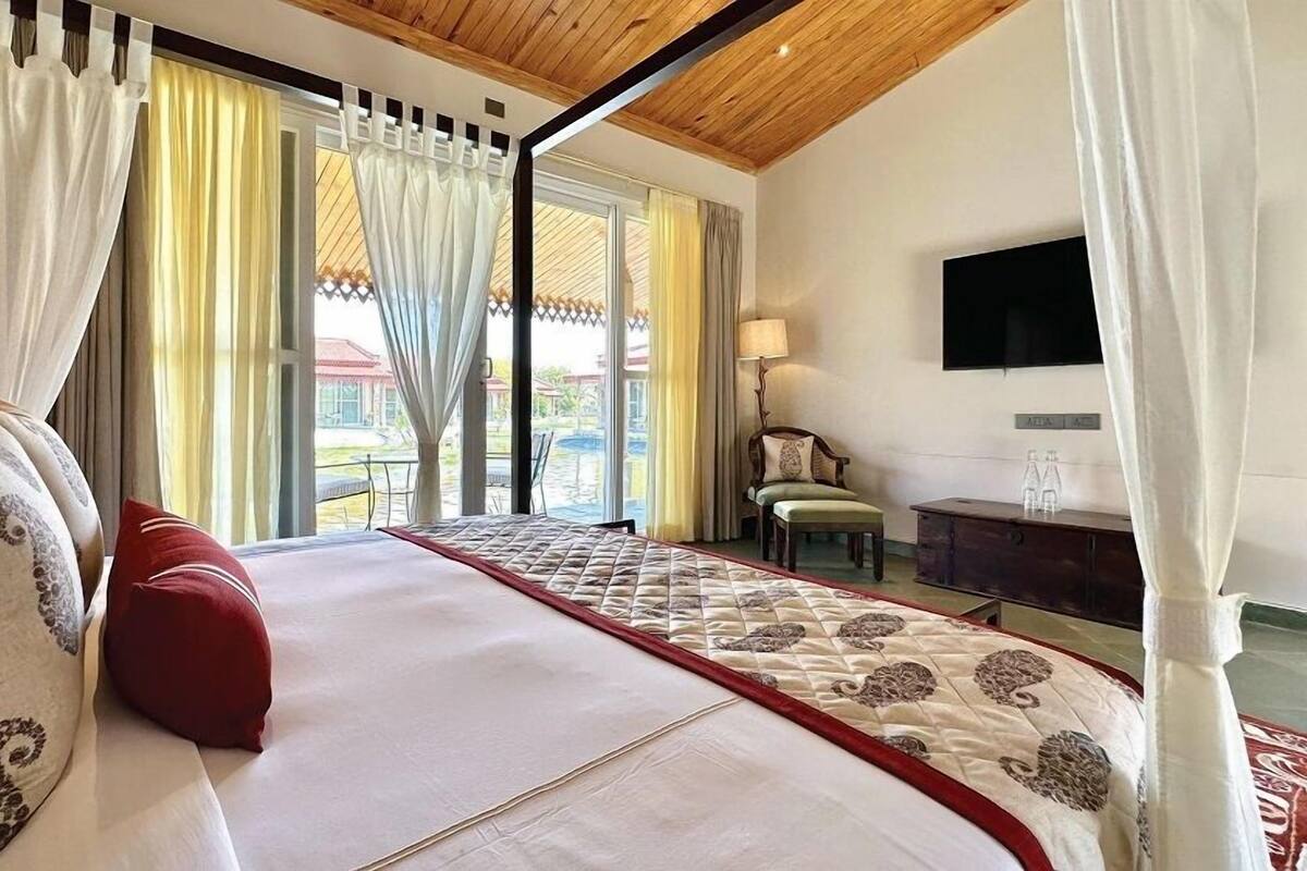 Quarto com cama grande, cortinas, televisão, escrivaninha e vista para o exterior.