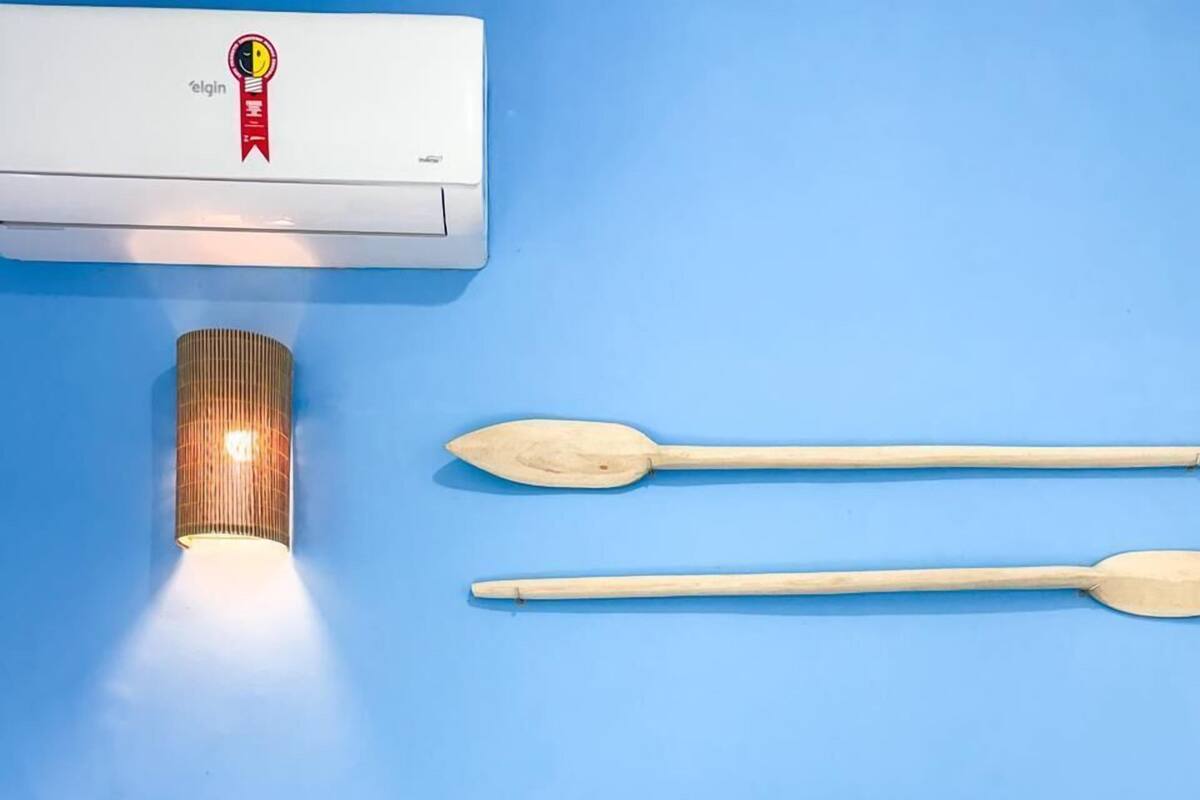 Quarto de hotel com cama, almofadas, mesa de cabeceira com telefone, ar-condicionado fixado na parede e luminária.