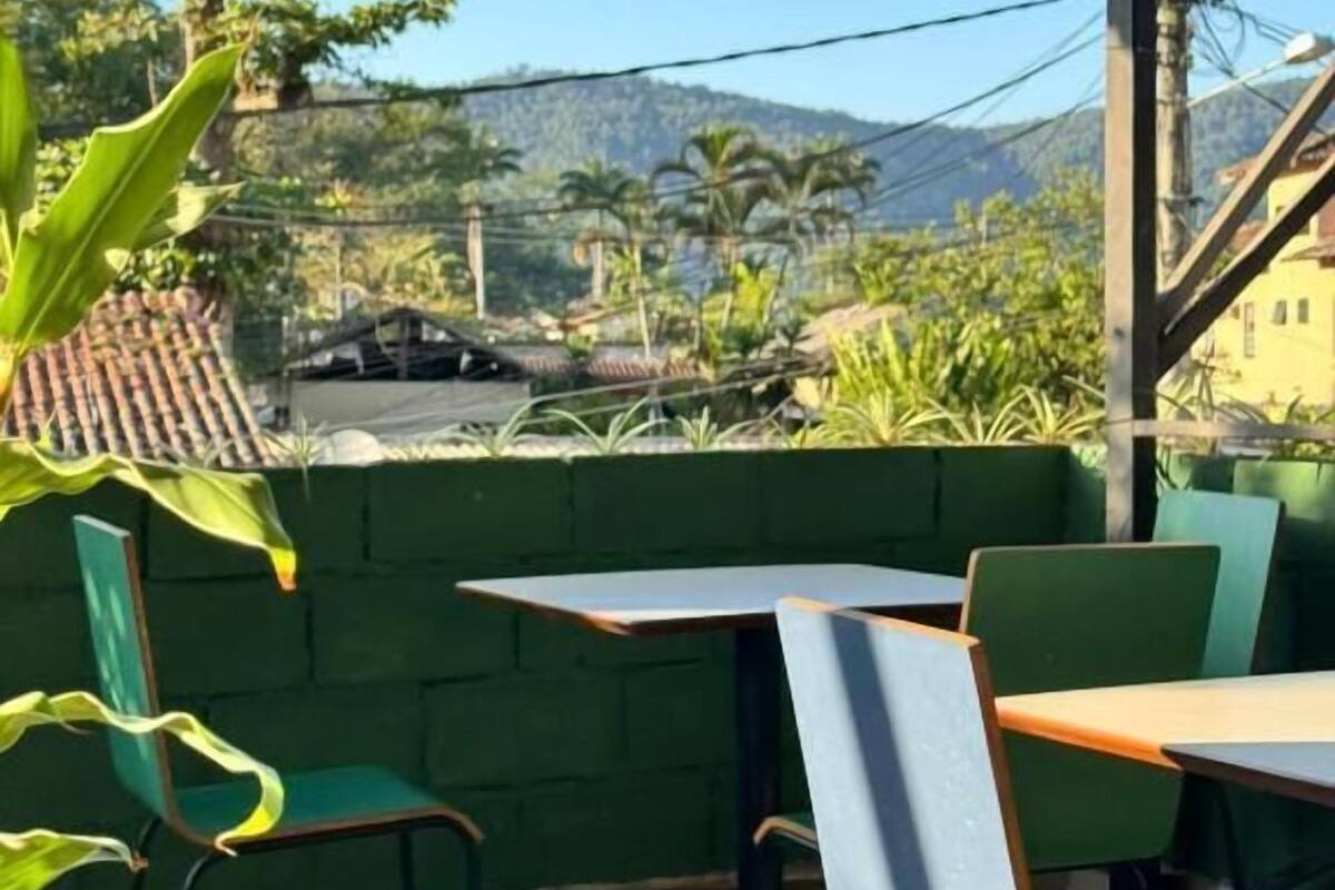 Um café ao ar livre com assentos acolchoados em tons de verde, piso de azulejos e vista para uma paisagem montanhosa.