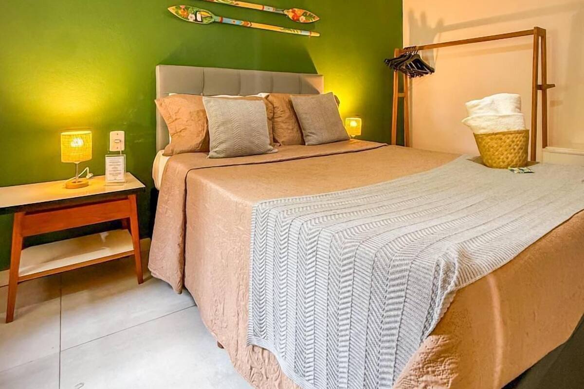 Quarto com cama, mesas de cabeceira, luminária pendente e prateleira na parede.