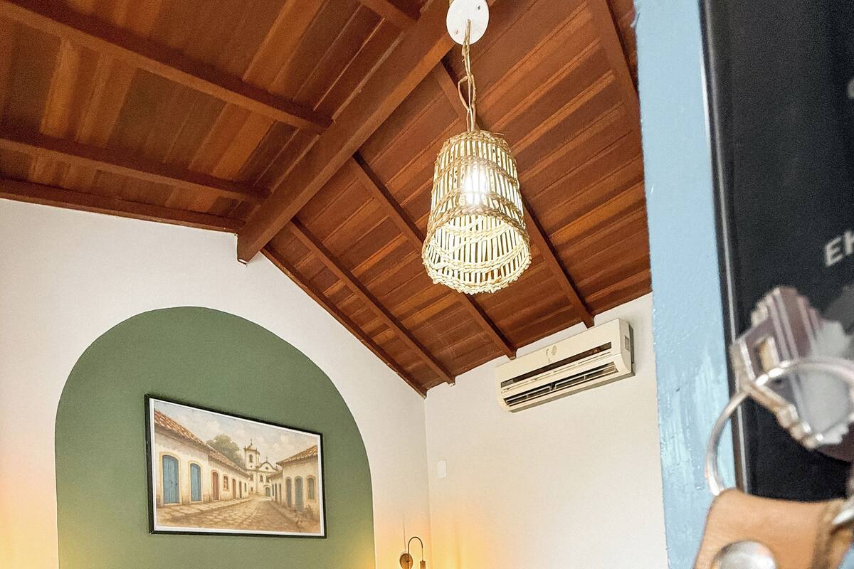 Quarto com cama, um quadro na parede e luminária suspensa.