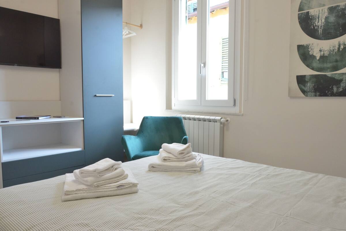 Quarto de hotel com uma cama, uma cadeira, uma televisão e uma janela.