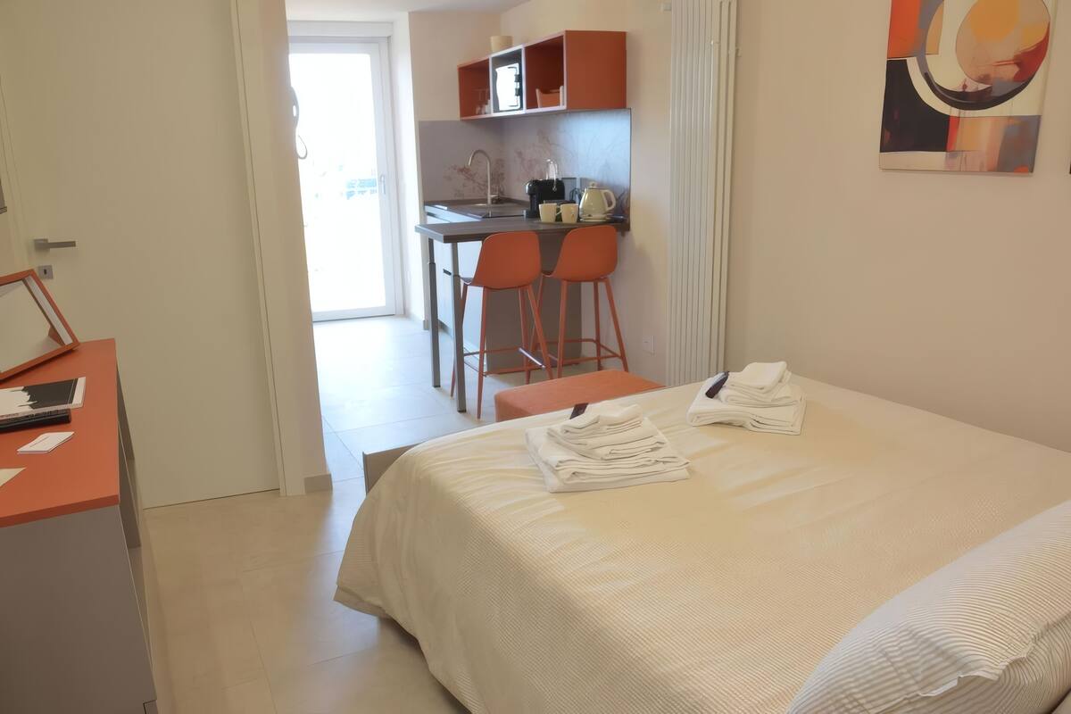 Quarto de hotel com cama, escrivaninha com cadeira, cozinha compacta e vista exterior.