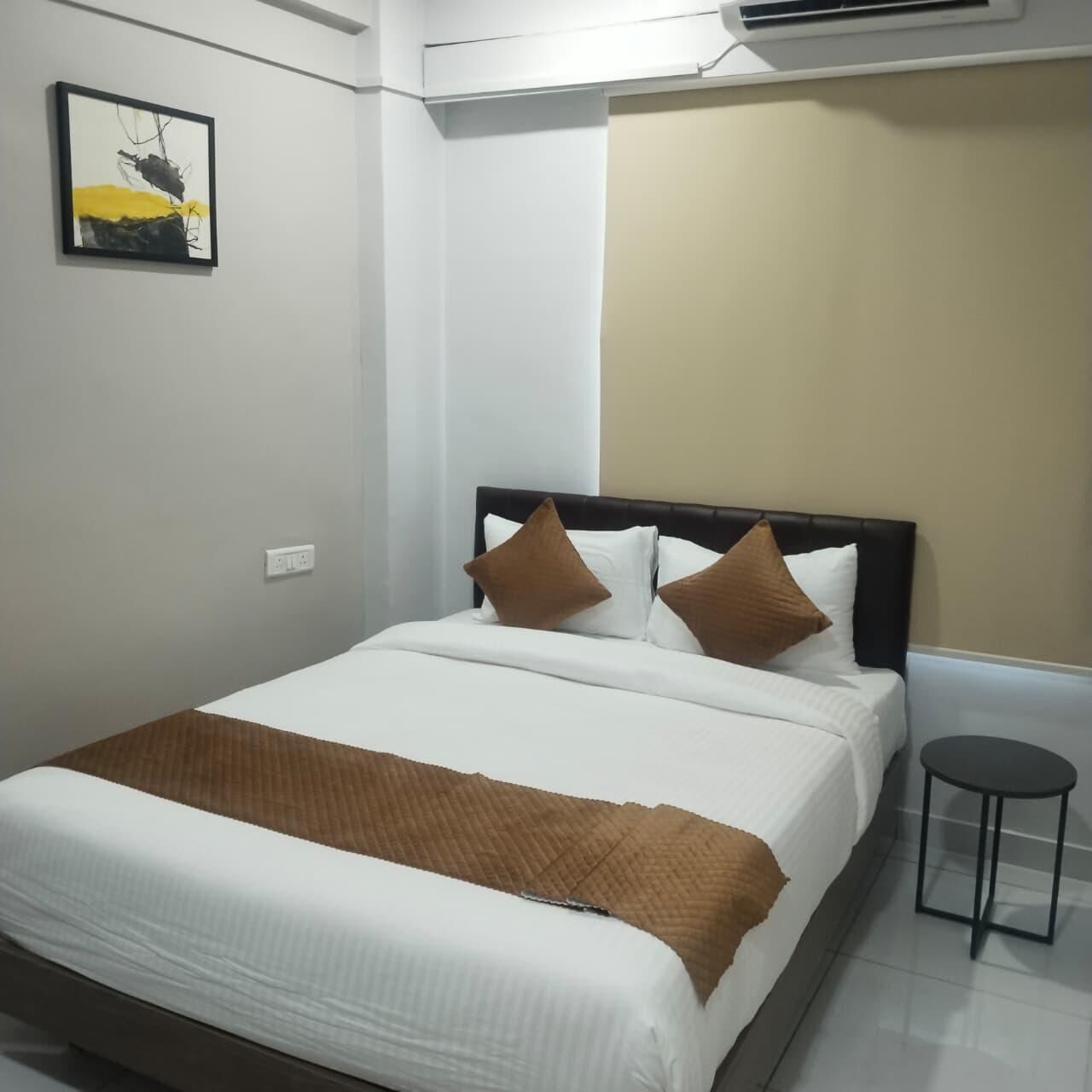 Quarto de hotel com cama, uma mesinha e um quadro na parede.