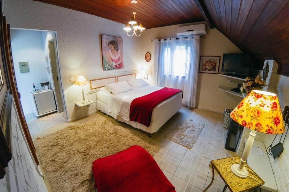Um quarto com uma cama, uma TV, um abajur e uma cadeira vermelha.