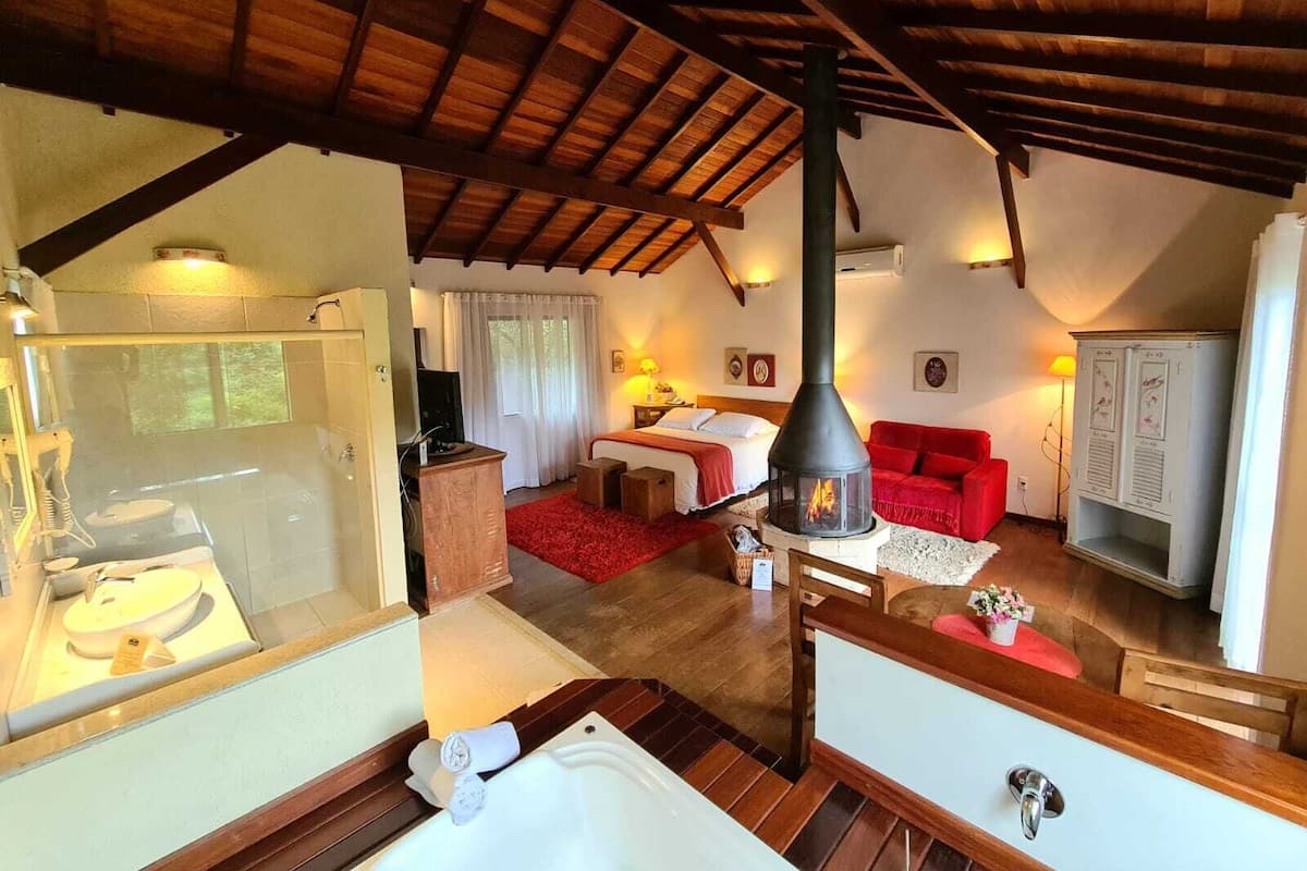 Um quarto acolhedor com lareira, uma cama, um sofá vermelho e uma mesa pequena com abajur.