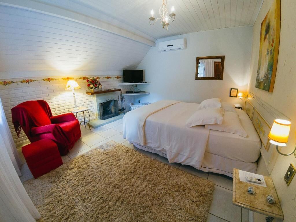 Quarto com cama, uma cadeira vermelha, televisão e lareira.