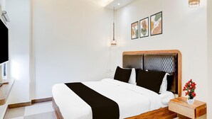 Quarto de hotel moderno com uma cama grande, cabeceira de madeira, mesa de cabeceira com um vaso de flores e luminária fixada na parede.