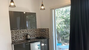 Uma cozinha compacta com geladeira, fogão e pia, um tapete estampado e vista através de uma porta de vidro deslizante.