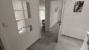 Um corredor com piso de azulejos, uma porta com espelho e um quadro na parede.
