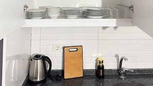 Cozinha com armários brancos, bancada preta, chaleira, porta-facas e pia.