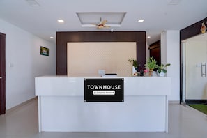 Uma receção com uma placa a indicar 'TOWNHOUSE Company-Serviced', um ventilador de teto, uma parede estampada e uma planta em vaso.