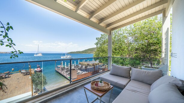 Uma varanda com vista para o mar, um deck de madeira e um sofá com almofadas.