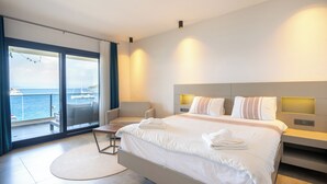 Quarto de hotel moderno com uma cama grande, área de estar e varanda vista para o mar.