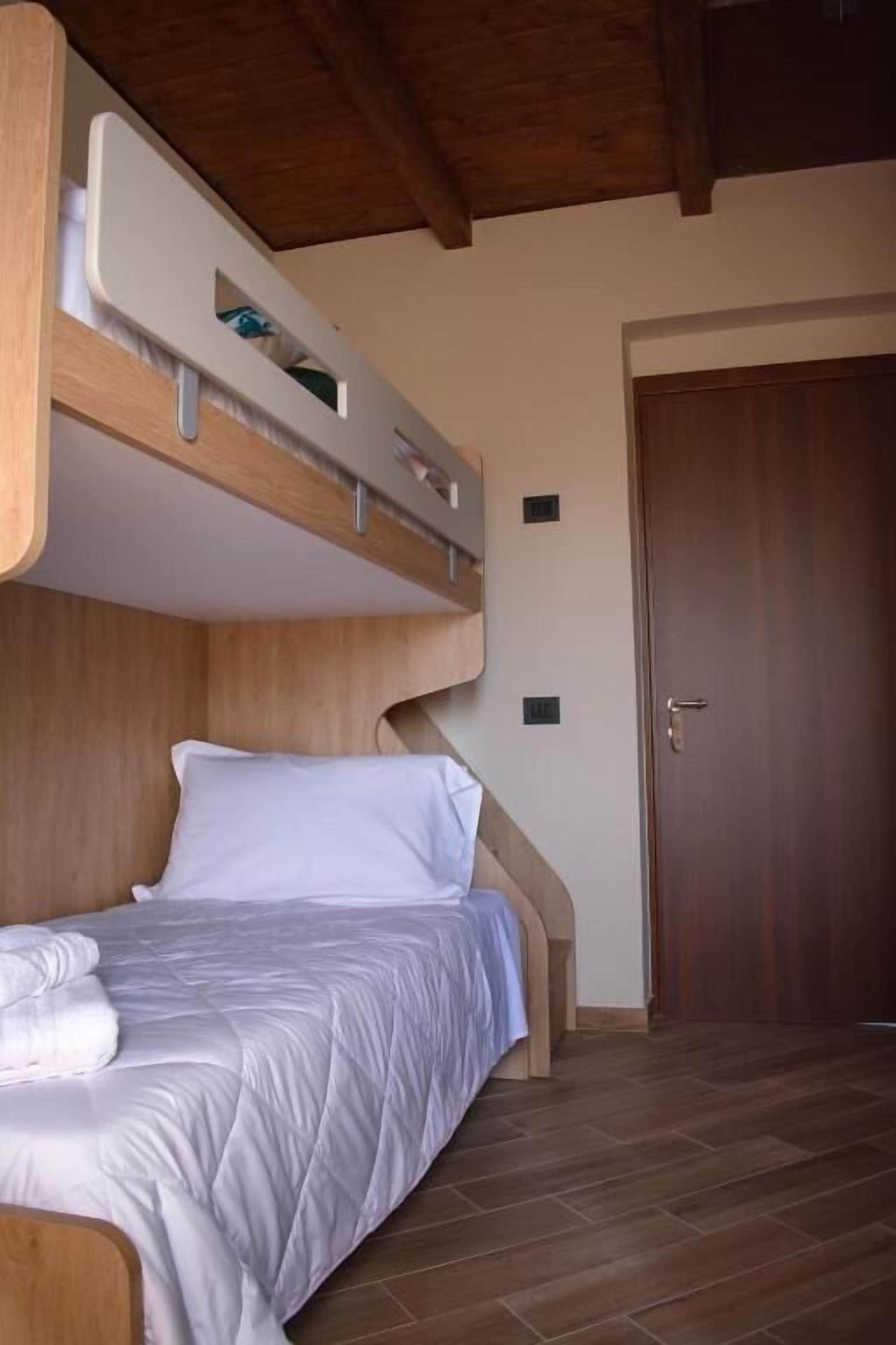 Uma cama beliche com cabeceira de madeira, colchão branco e prateleira de madeira em cima.