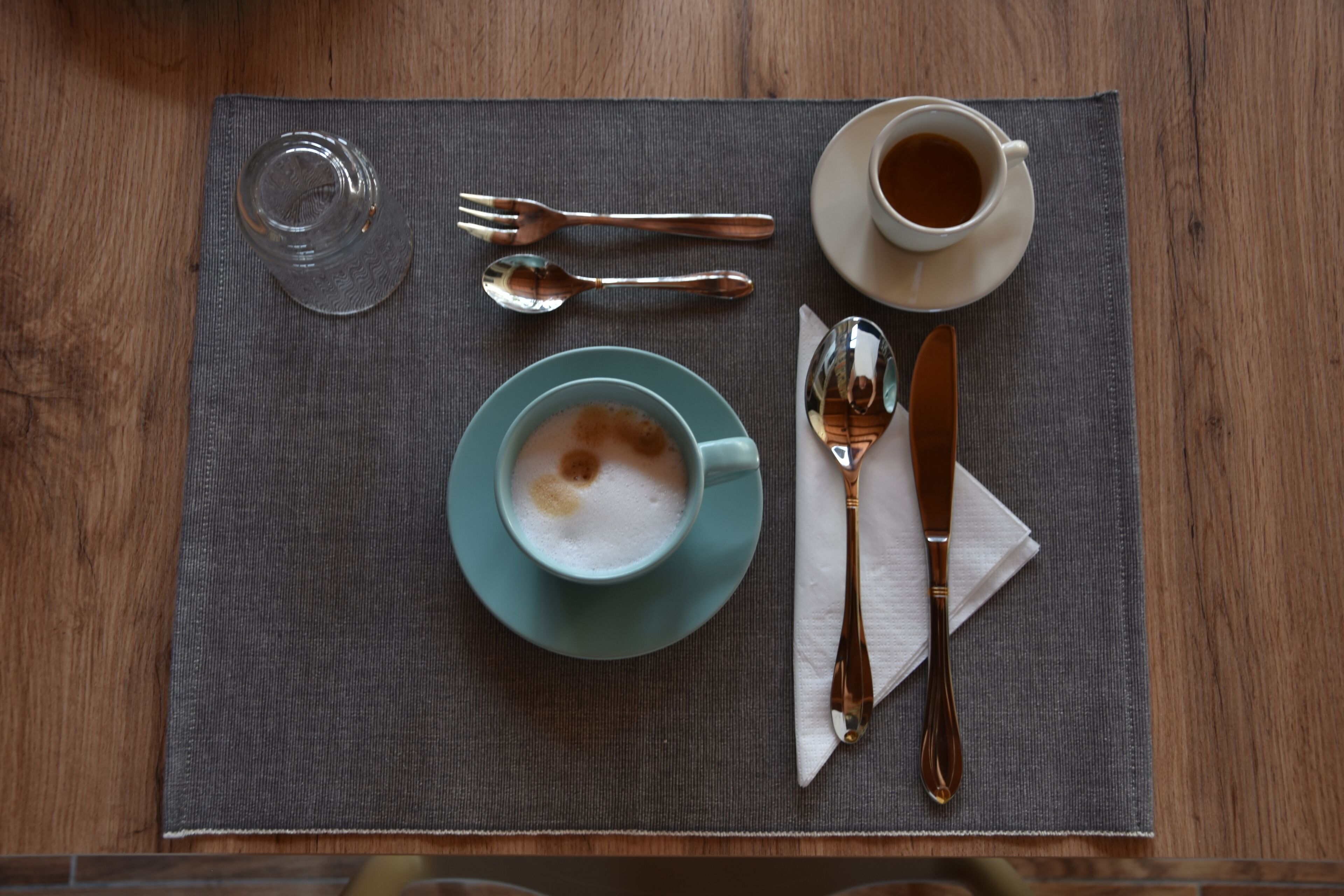 Uma mesa com uma chávena de café, um copo e talheres sobre um guardanapo.