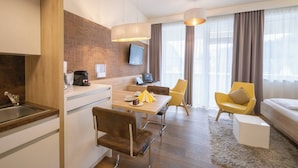 Quarto de hotel moderno com área de jantar, sofá e TV fixada na parede.