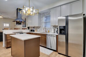 Uma cozinha moderna com ilha central, eletrodomésticos de aço inoxidável e uma luminária geométrica singular.