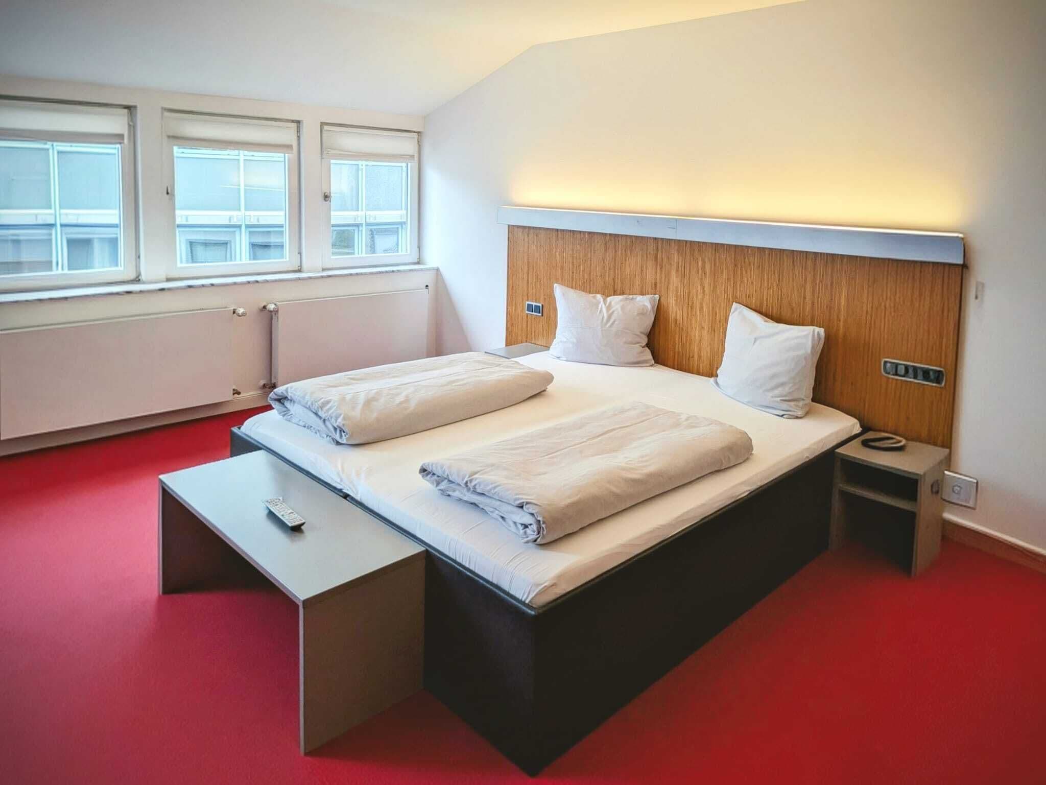 Quarto de hotel moderno com cama, mesas de cabeceira, escrivaninha e janela.