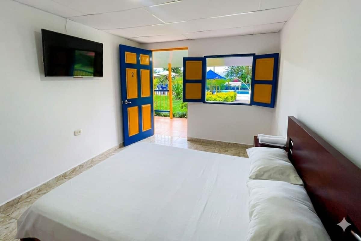 Quarto com cama, televisão presa na parede e porta que dá para área externa.