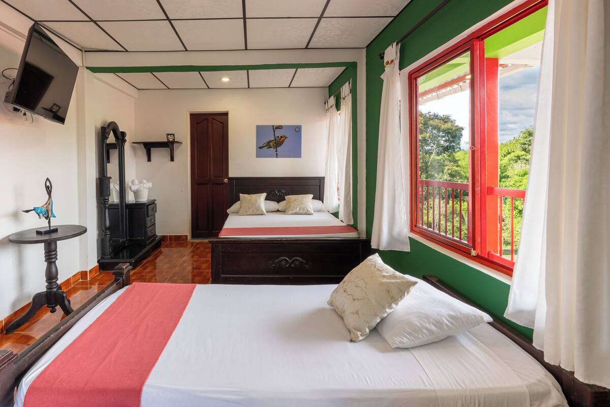 Quarto de hotel com duas camas, televisão de tela plana, pintura e janela com vista para área verde.